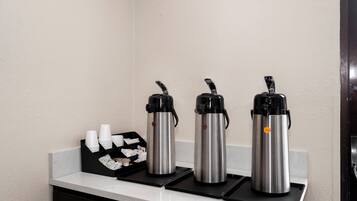 Uma bancada com dois distribuidores de café de aço inoxidável e uma caixa de copos descartáveis.