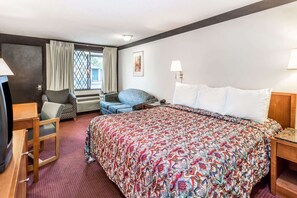 Quarto de hotel com uma cama grande, uma escrivaninha, uma cadeira e uma janela com cortinas.