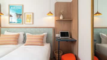 Quarto de hotel com duas camas, um laptop sobre uma mesinha, um quadro emoldurado de Marselha e um espelho.