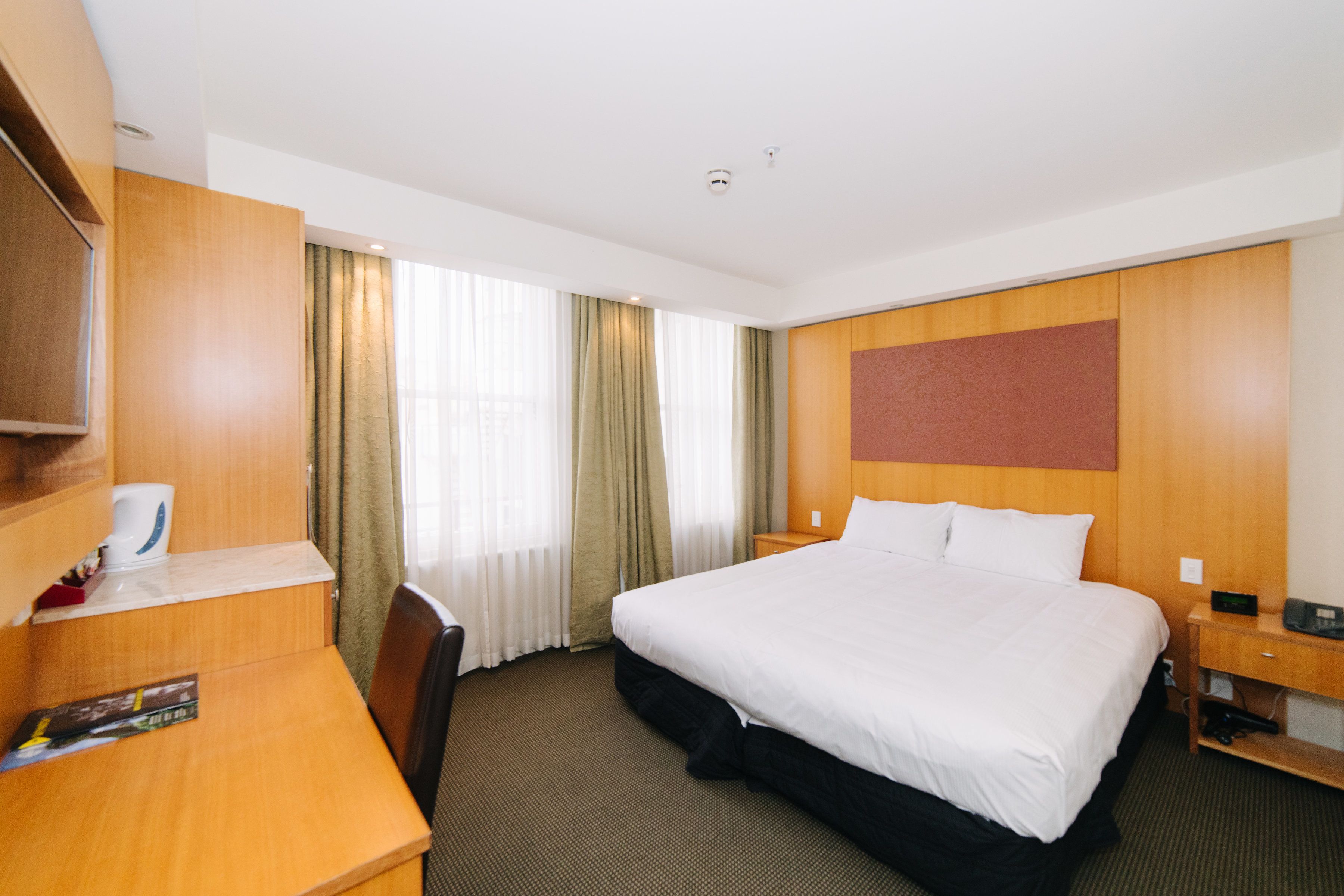 Quarto de hotel com uma cama grande, uma escrivaninha, uma cadeira, uma cafeteira e uma mesa de cabeceira com um telefone.