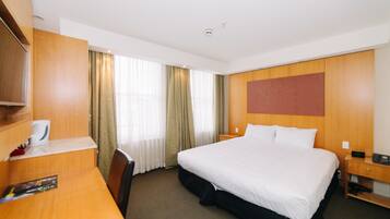 Quarto de hotel com uma cama grande, uma escrivaninha, uma cadeira, uma cafeteira e uma mesa de cabeceira com um telefone.