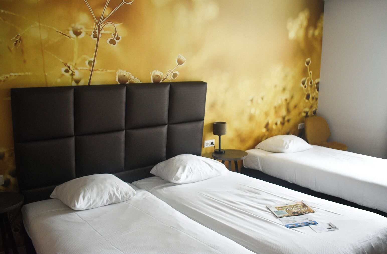 Quarto de hotel com duas camas, uma cabeceira escura e uma parede com padrão floral.