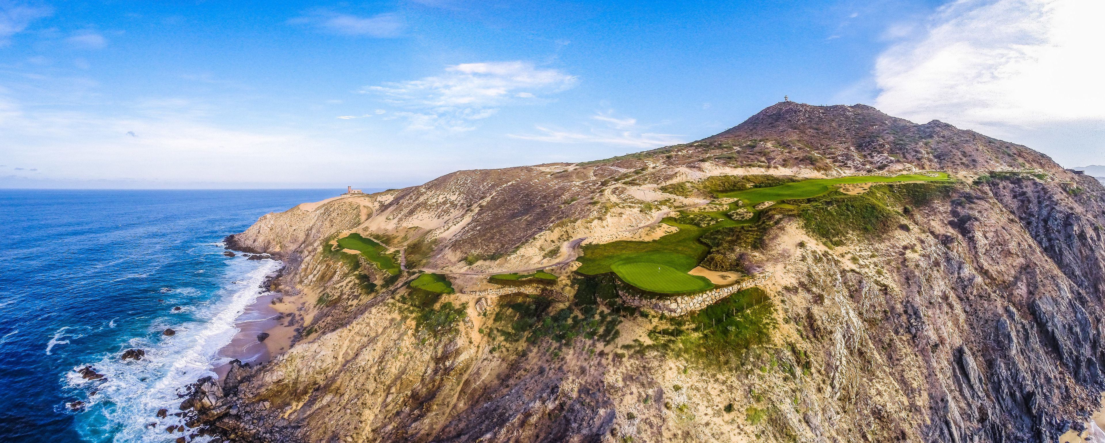 Paisagem costeira com penhascos rochosos, um campo de golfe e um farol.