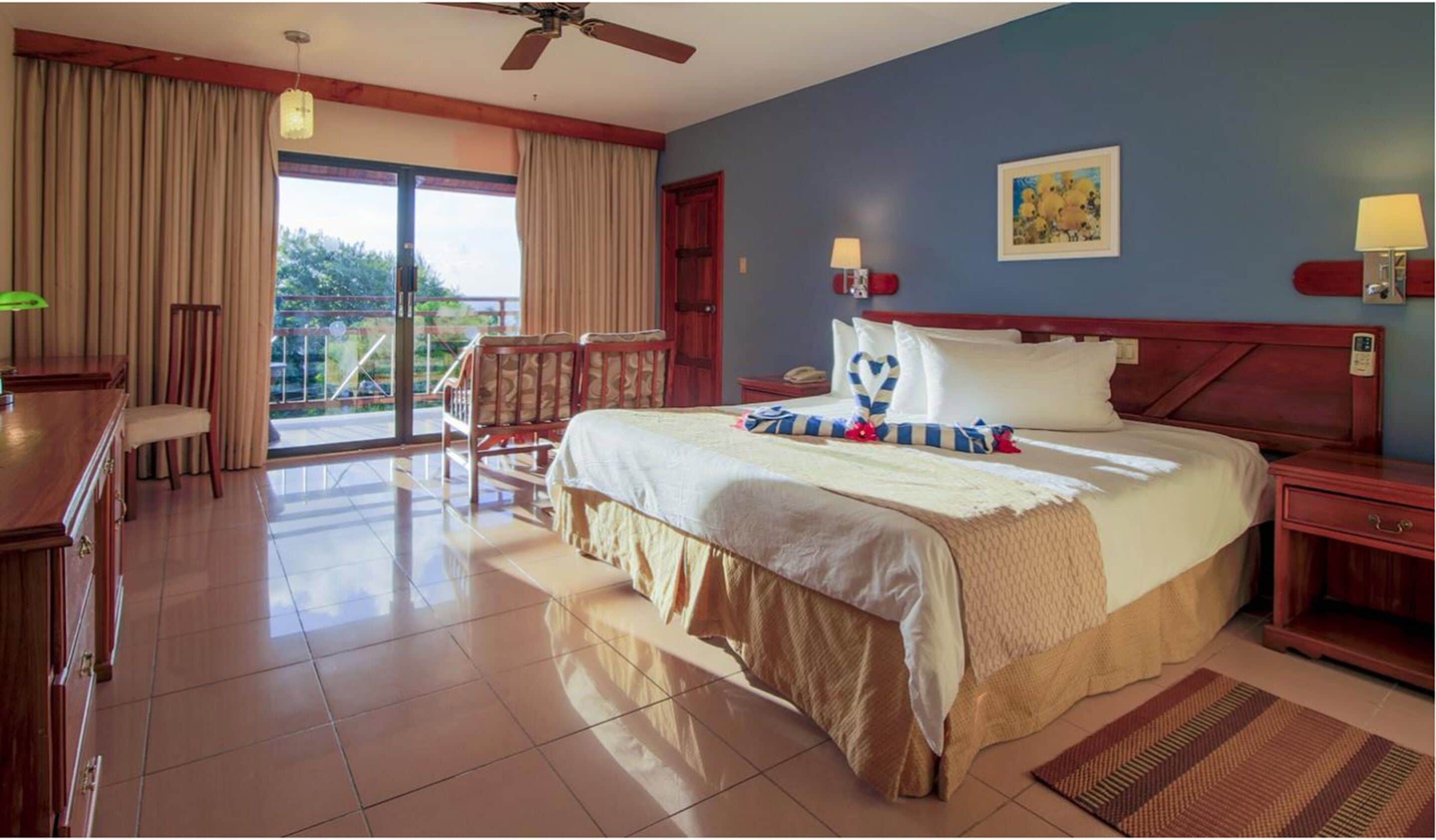 Quarto de hotel com uma cama grande, uma escrivaninha, uma cadeira, varanda e um quadro na parede.