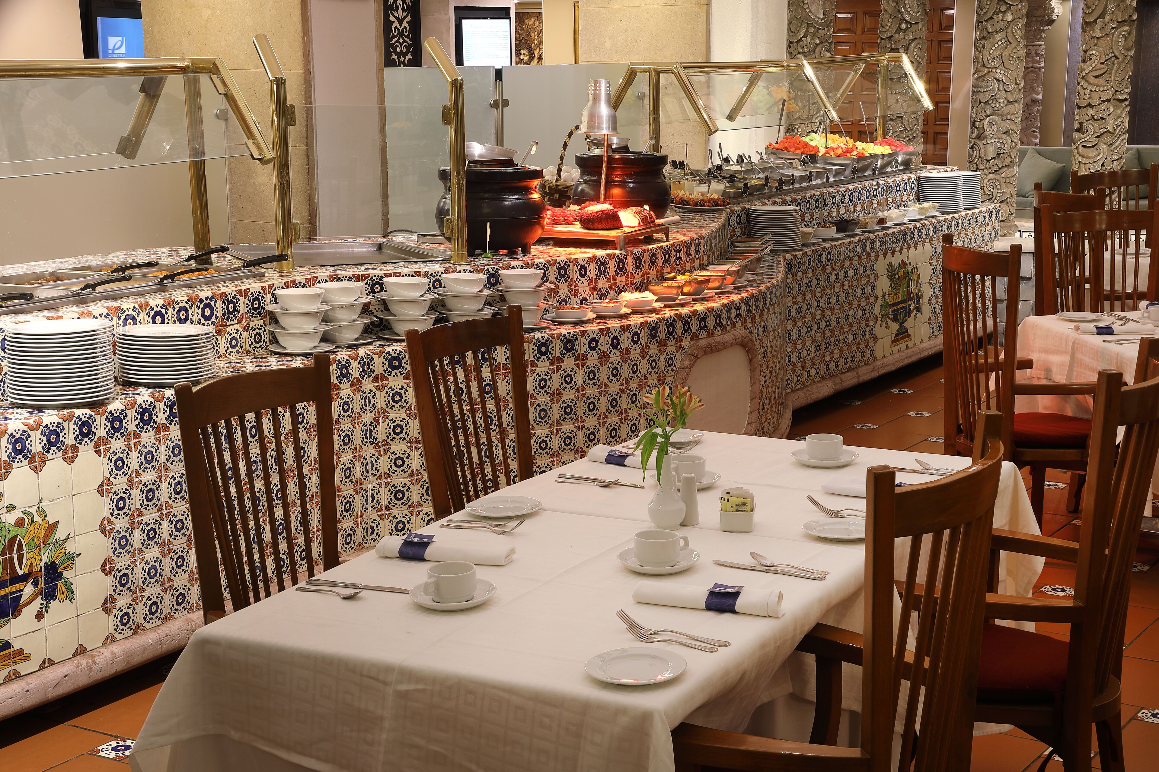 Disposição de buffet com diversas estações de serviço, variedade de pratos e mesas de jantar organizadas com cadeiras.