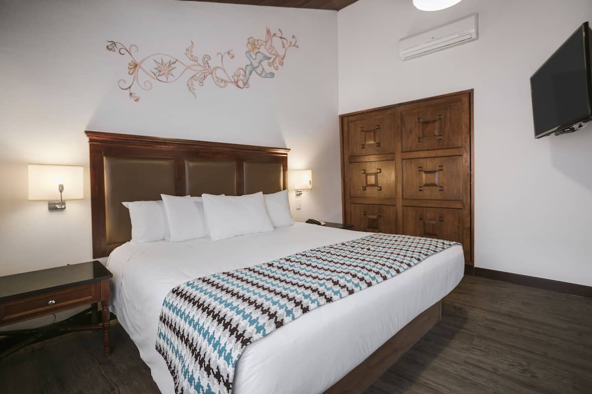 Quarto de hotel com uma cama grande, cabeceira de madeira, duas mesas de cabeceira, um guarda-roupa e uma televisão de tela plana na parede.