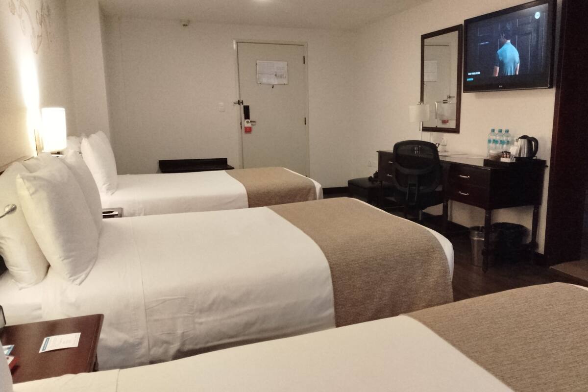 Quarto de hotel com duas camas, uma escrivaninha, uma cadeira, uma televisão e uma porta com aviso.