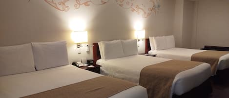 Quarto de hotel com três camas, cada uma com roupa de cama branca e cabeceiras marrons. Há luminárias e telefone nas mesas de cabeceira.