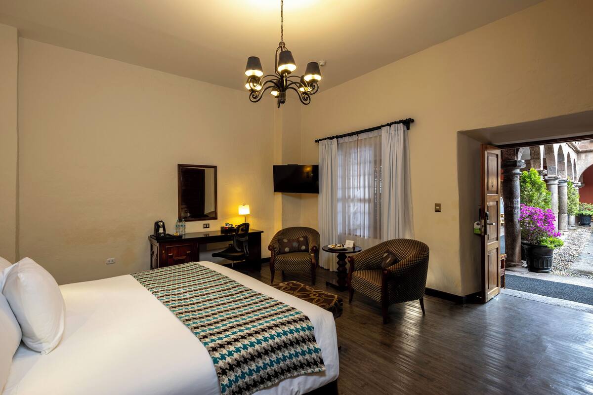 Quarto de hotel com cama, escrivaninha, cadeira, televisão e vista para o exterior.