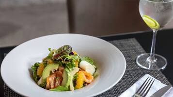 Um prato branco com salada, um copo de vinho branco e um garfo sobre uma mesa.