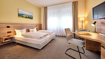 Quarto de hotel com cama, escrivaninha com cadeira, televisão e um quadro na parede.