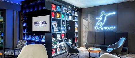 Um saguão de hotel moderno, com a placa Novotel, uma placa de neon e uma exposição de itens colecionáveis esportivos.