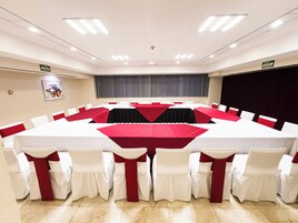 Uma sala de conferências com uma grande mesa retangular, cadeiras brancas com fitas vermelhas e toalha de mesa preta.