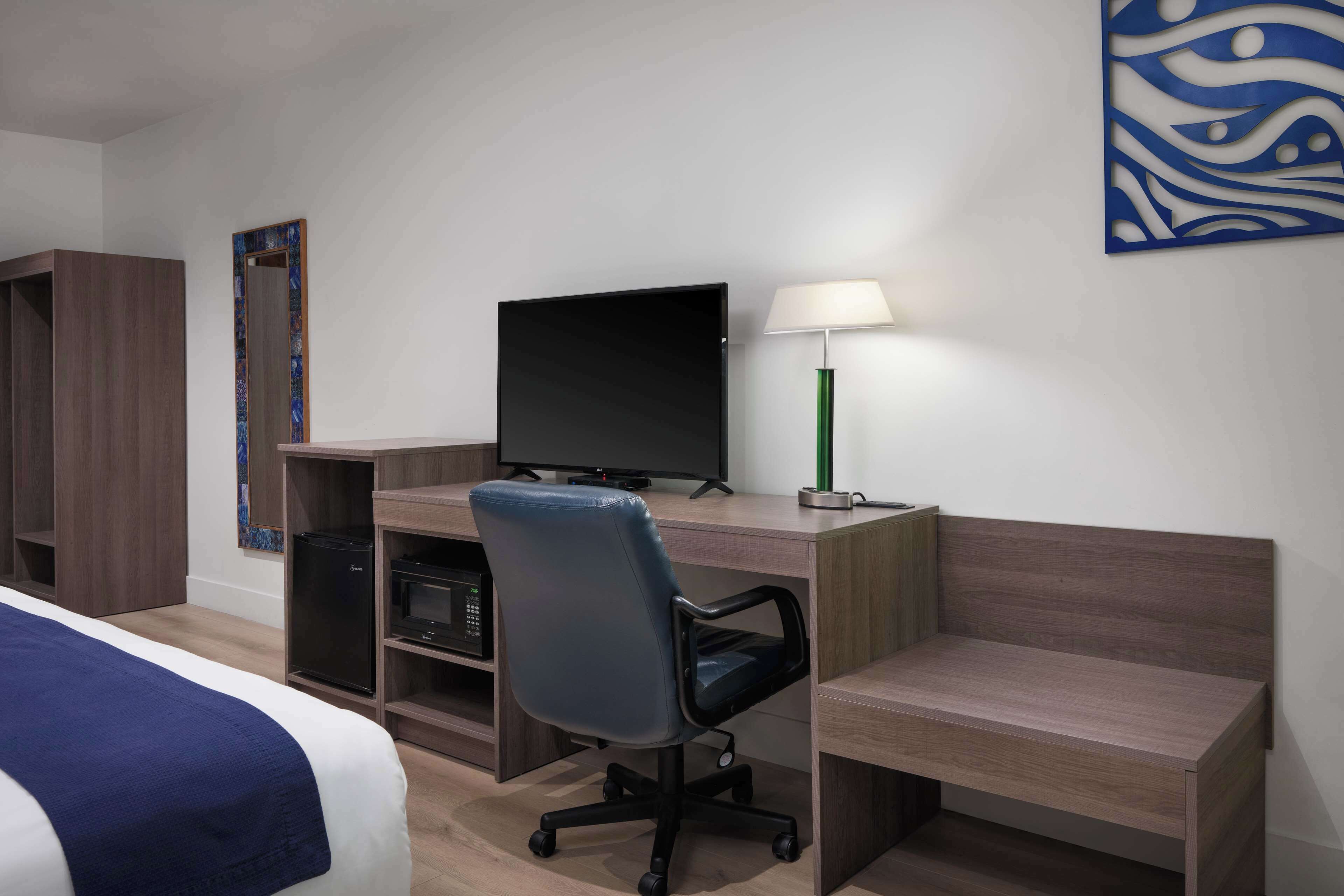Quarto de hotel com cama, escrivaninha com computador, cadeira, televisão, abajur e armário.