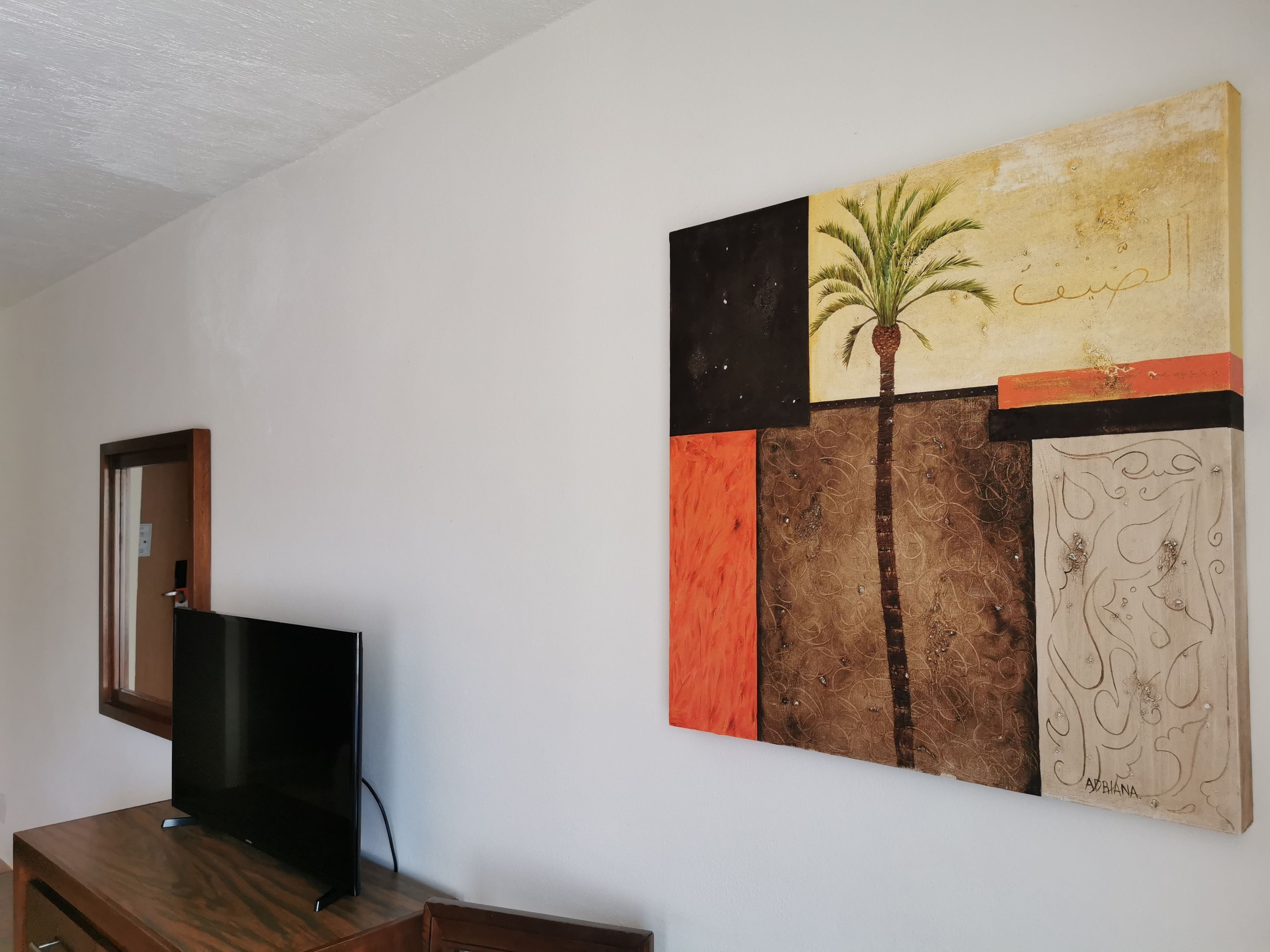 Quarto com televisão de tela plana em suporte de madeira, um quadro na parede e uma porta com espelho.