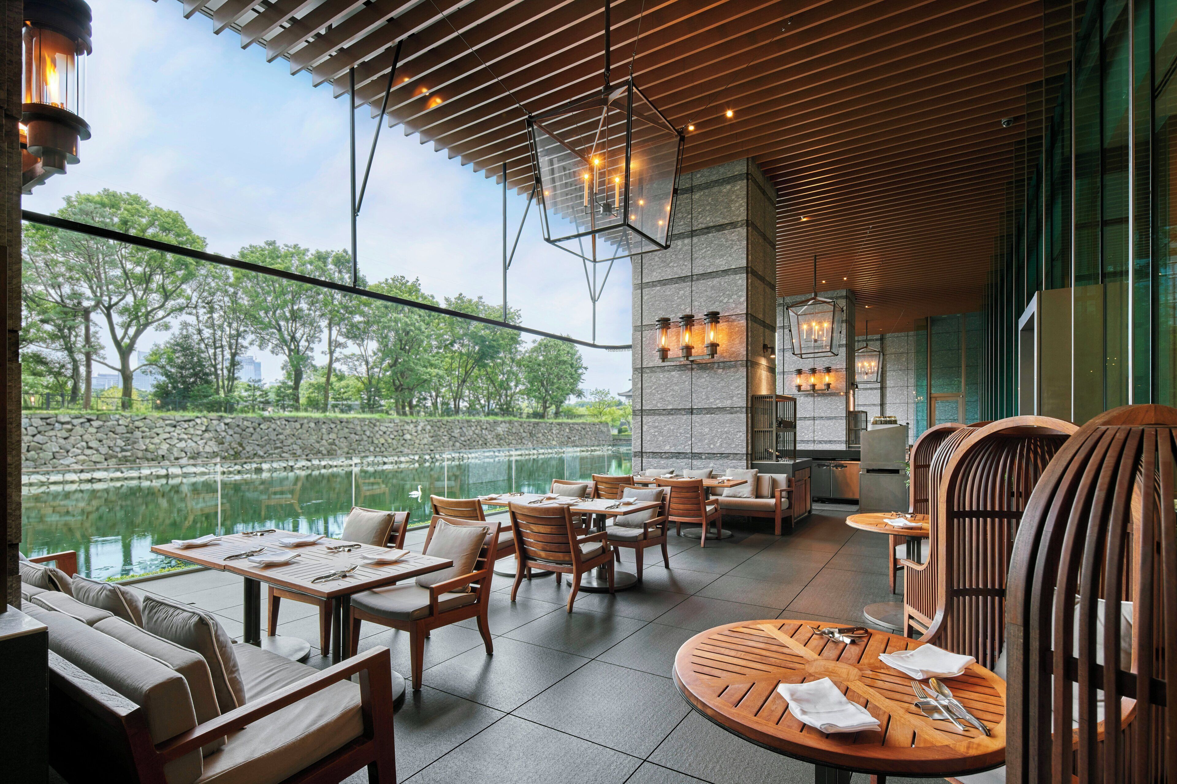 Restaurante com área externa e mesas ao ar livre, com vista para a água, móveis modernos e iluminação ambiente.