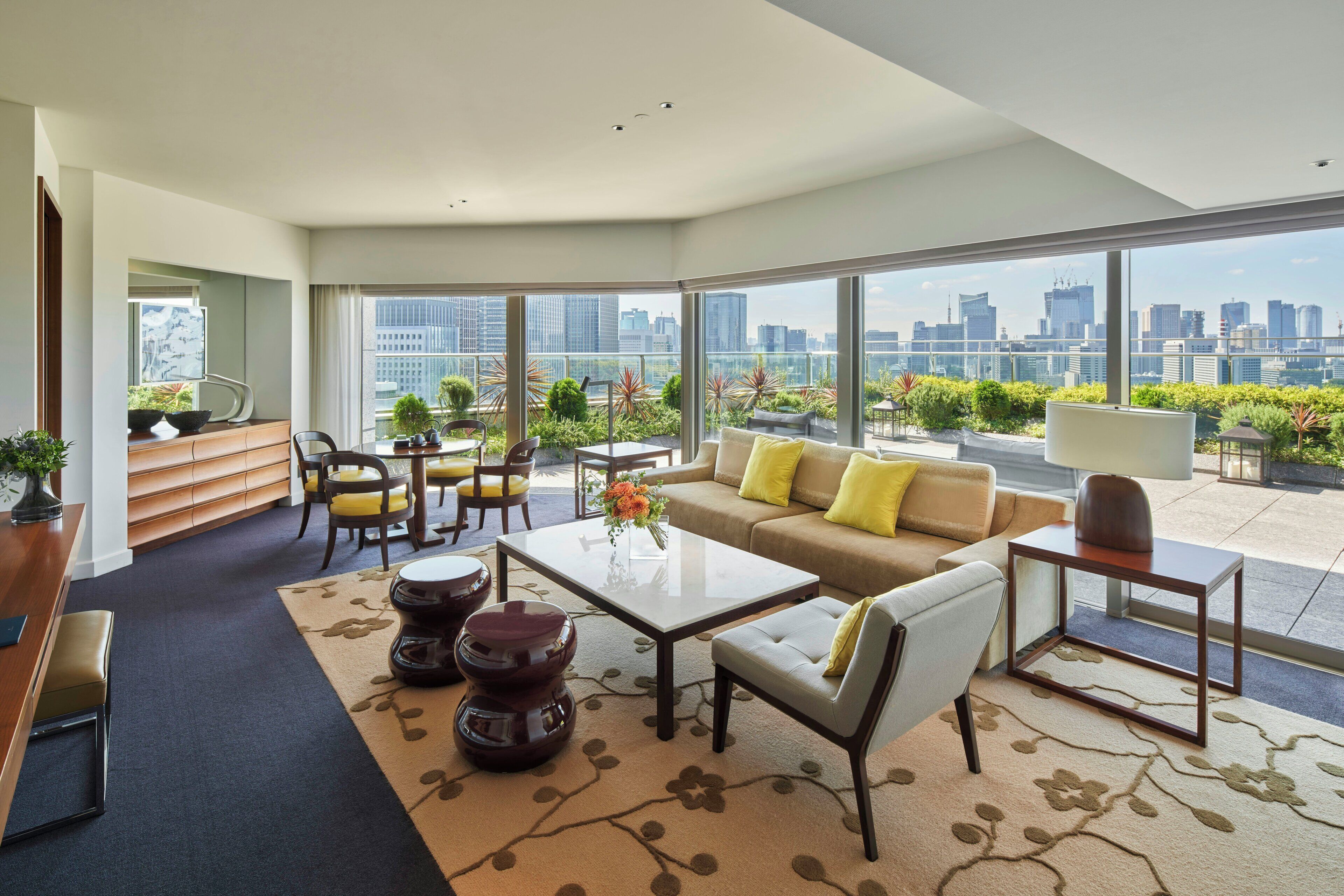 Uma sala de estar moderna com vista para a cidade, com um sofá, mesa de centro, cadeiras e área de jantar.