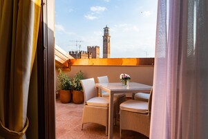 Varanda com móveis de vime, plantas em vasos e vista para uma torre histórica.