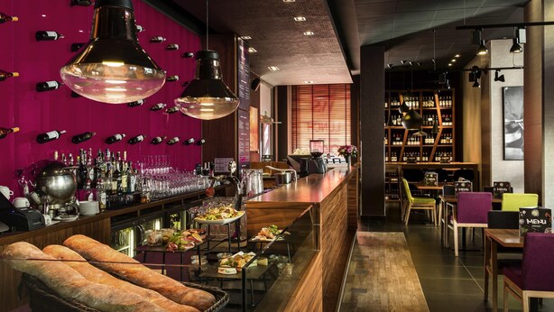 Uma área de bar com balcão de madeira, garrafas de vinho e diversos alimentos.
