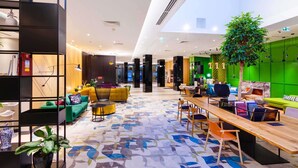 Um lobby moderno com balcão de recepção, áreas de estar, uma planta grande e um chão com padrão.