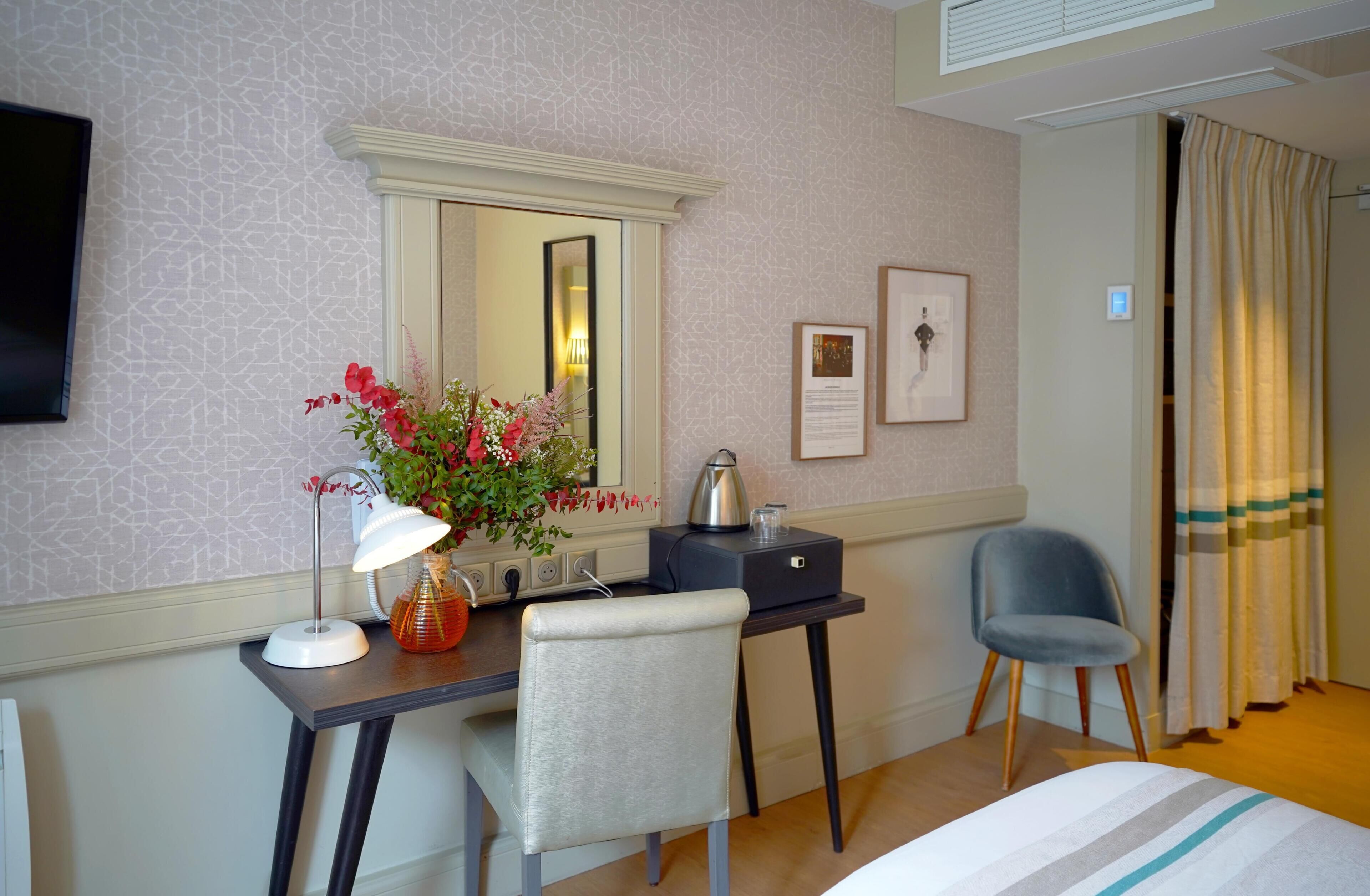 Quarto de hotel com escrivaninha, cadeira, cama, televisão e espelho.