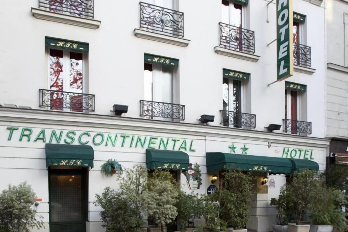 Um hotel com toldo verde, um letreiro indicando 'Transcontinental Hotel' e uma varanda com guarda-corpo.