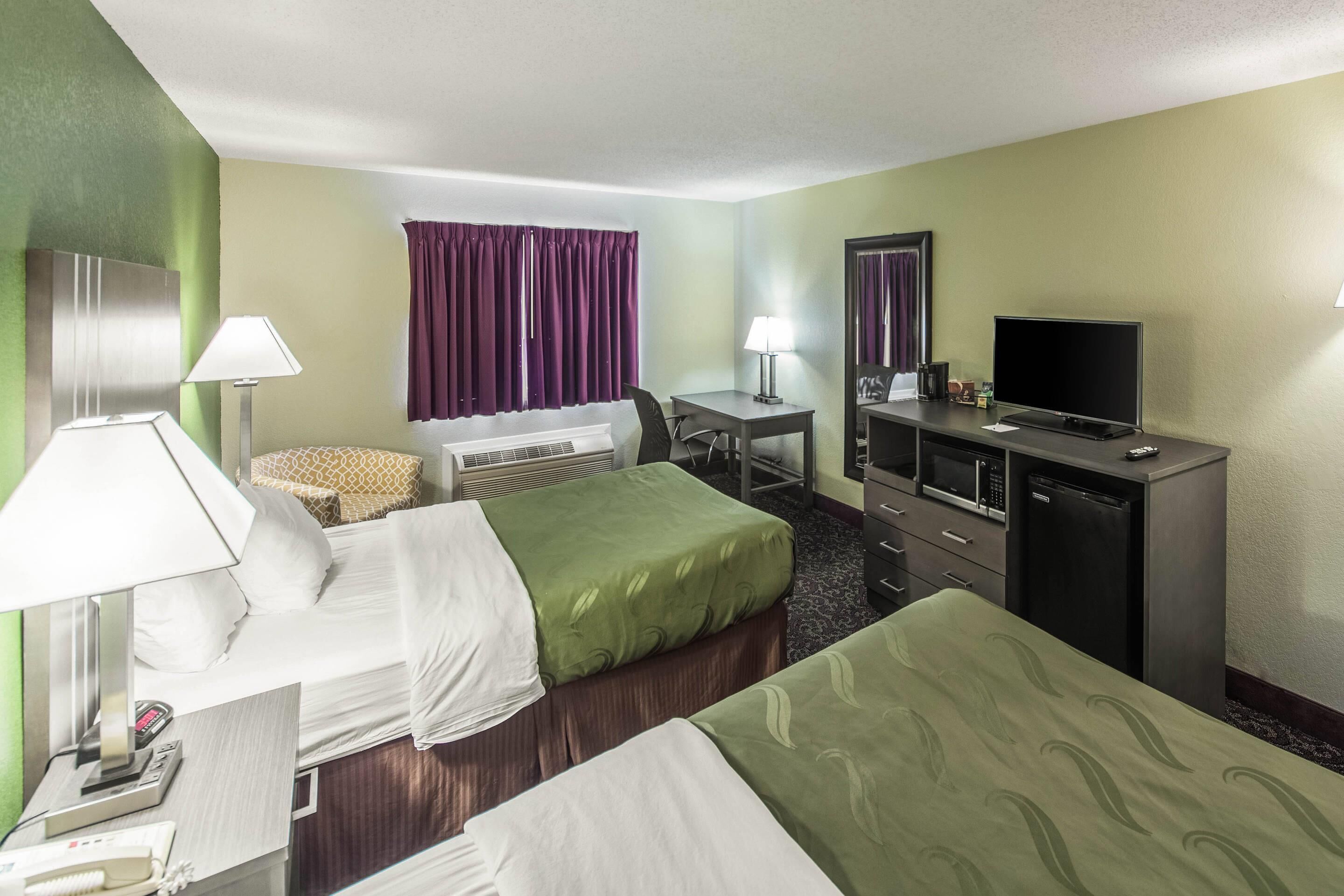 Quarto de hotel com duas camas, uma escrivaninha, televisão, micro-ondas e cómoda.