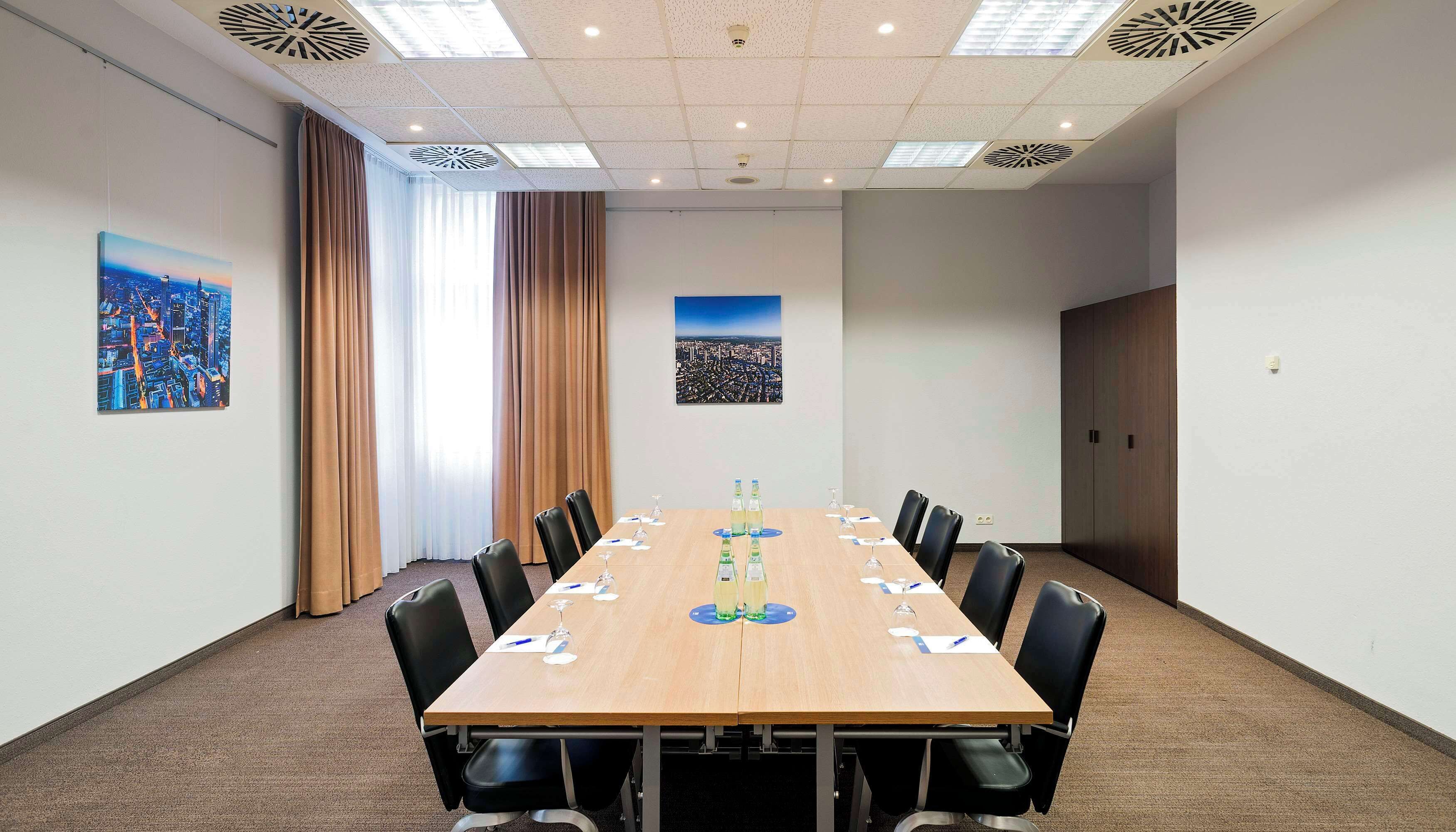 Uma sala de conferência com uma mesa comprida, cadeiras pretas e duas pinturas nas paredes.