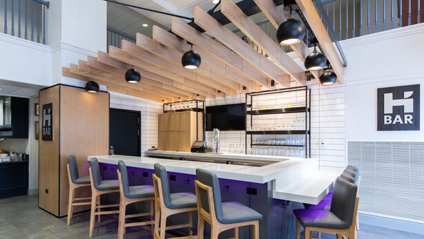 Uma área de bar moderna com balcão de madeira, banquetas e iluminação pendente.