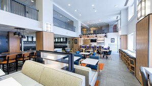 Um espaço amplo e interno com vários arranjos de assentos, incluindo cabines e mesas, uma escadaria conectando diferentes níveis e uma área de bar visível.