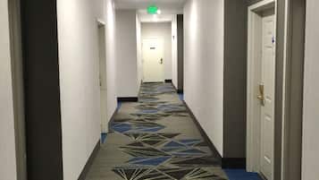 Um corredor de hotel com carpete estampado, paredes brancas e portas em ambos os lados.