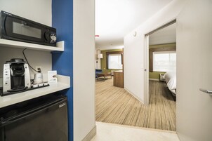 Quarto de hotel com cozinha compacta, uma cama, uma janela e uma porta que dá para outro quarto.