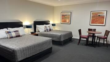 Quarto de hotel com duas camas, uma mesinha com cadeiras e dois quadros na parede.