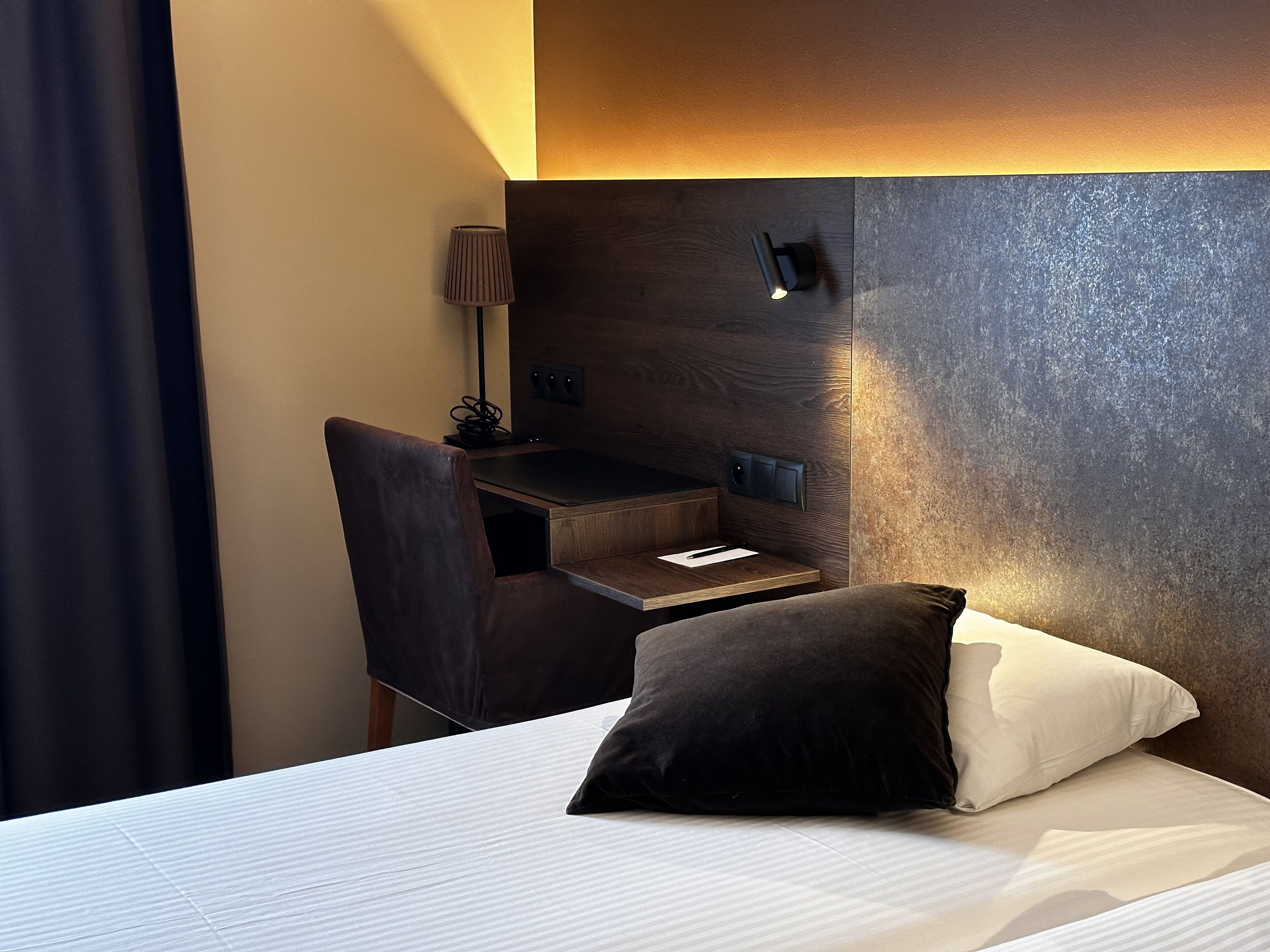 Quarto de hotel com cama, escrivaninha e abajur.