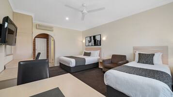 Quarto de hotel com duas camas, uma escrivaninha, uma cadeira, uma televisão e um ventilador de teto.