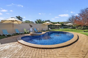 Uma piscina com um deck de tijolos, cadeiras de descanso e guarda-sóis.