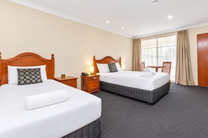 Quarto de hotel com duas camas, uma escrivaninha, uma cadeira e uma janela com cortinas.