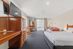 Quarto de hotel com cama, escrivaninha, cadeira, televisão e janela com cortinas.