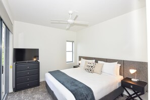 Quarto com cama, cômoda, televisão, ventilador de teto e mesa de cabeceira com luminária.