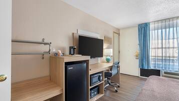 Quarto de hotel com cama, escrivaninha com computador, televisão, minibar e janela com cortinas.