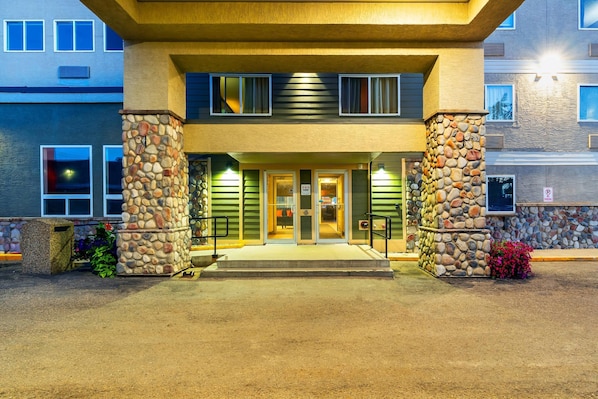 Entrada de hotel com fachada de pedra, cobertura e placa indicando área de estacionamento.