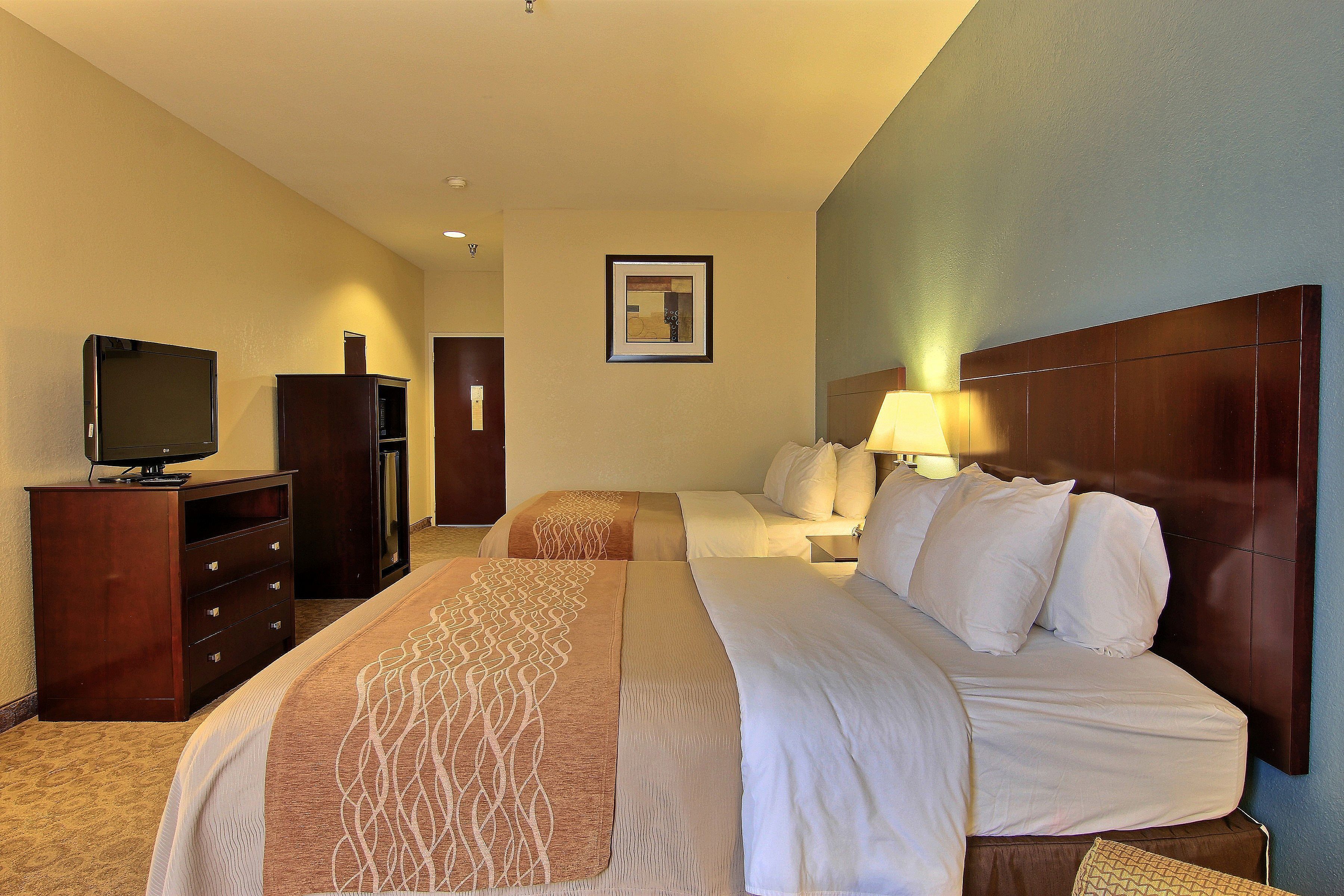 Quarto de hotel com uma cama grande, uma TV em uma cômoda e um quadro na parede.