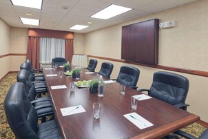 Uma sala de conferências com uma longa mesa de madeira, cadeiras de couro preto e uma tela de projetor na parede.