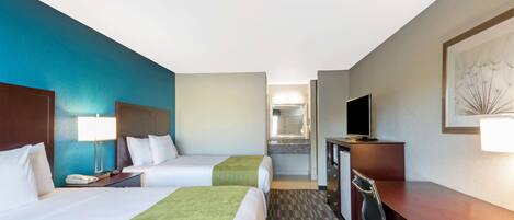 Quarto de hotel com duas camas, uma escrivaninha, televisão e banheiro visível por uma porta aberta.