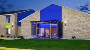 Um edifício com fachada de tijolos, toldo azul e área externa com mesas e cadeiras.