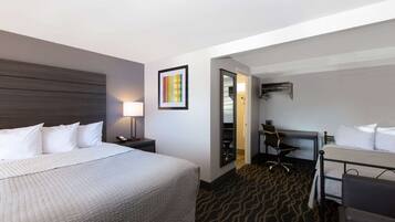 Quarto de hotel com uma cama grande, uma escrivaninha, uma cadeira, um abajur e um espelho.