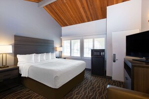 Quarto de hotel com cama grande, televisão, escrivaninha com abajur e minibar.
