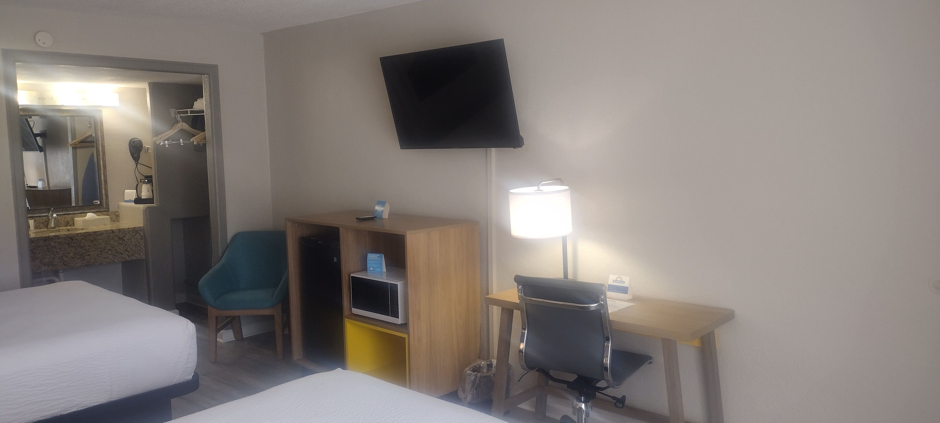 Quarto de hotel com cama, secretária e cadeira, televisão na parede, abajur e espelho.