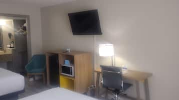 Quarto de hotel com cama, secretária e cadeira, televisão na parede, abajur e espelho.