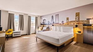 Quarto de hotel com cama, escrivaninha, cadeira, aquecedor e um mural com vista para a cidade.